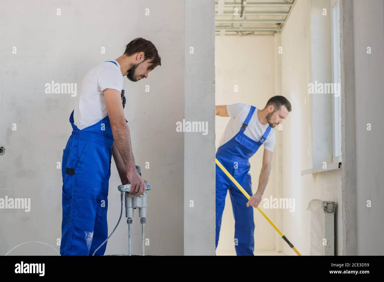 Two builders in blue overalls use construction tools Stock Photo - Alamy