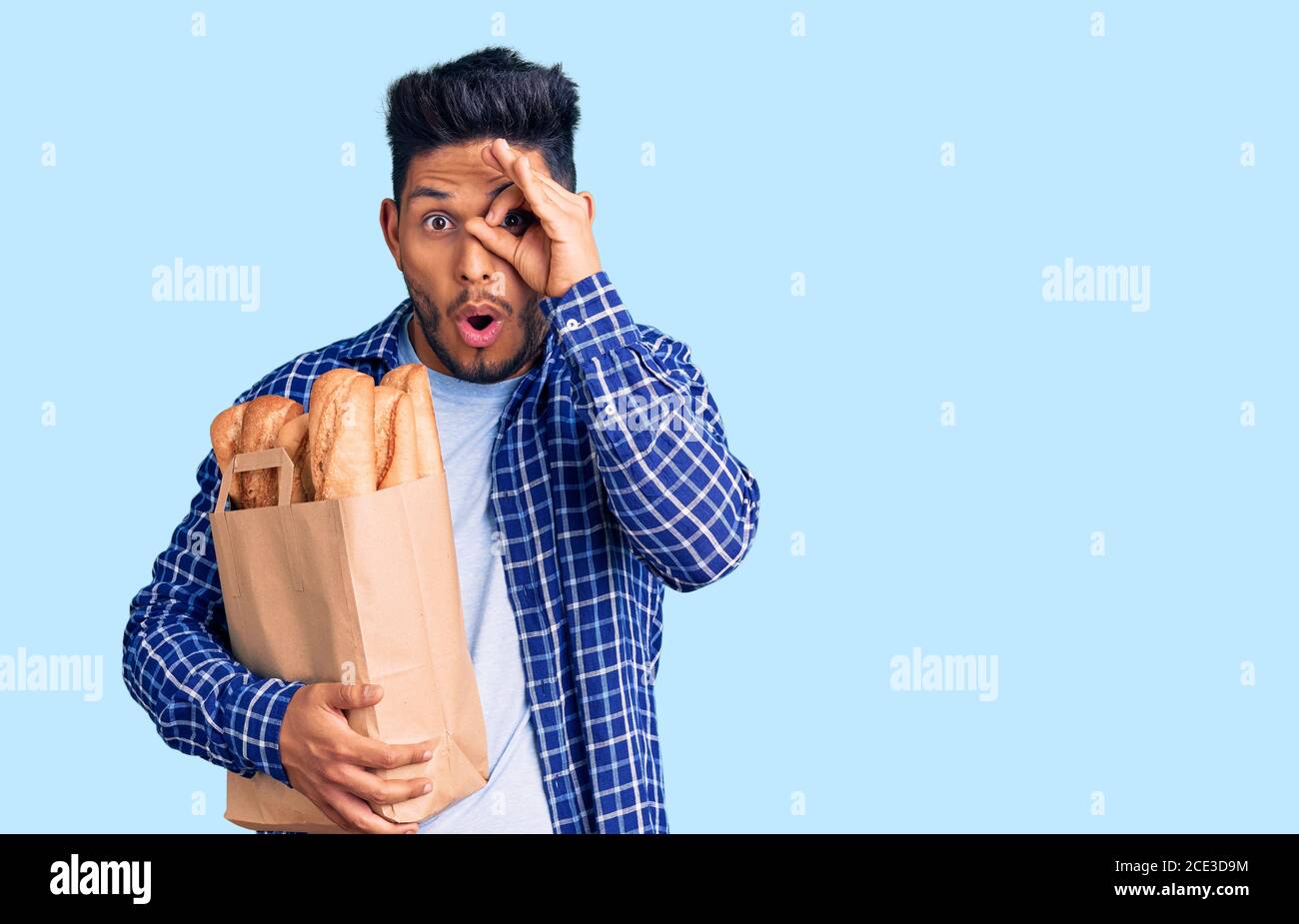 Handsome latin american young man holding paper bag with bread doing ok ...