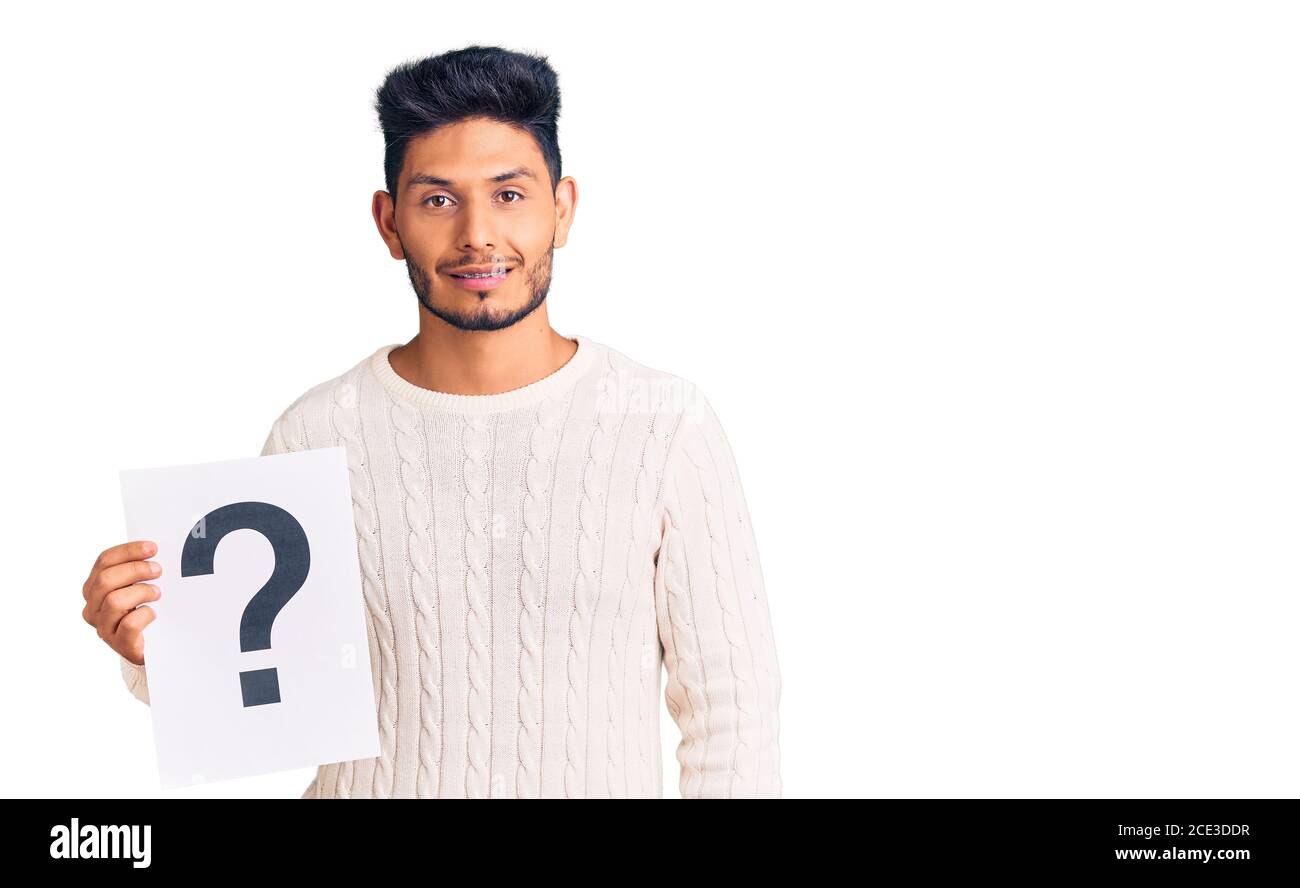 Handsome latin american young man holding question mark looking ...