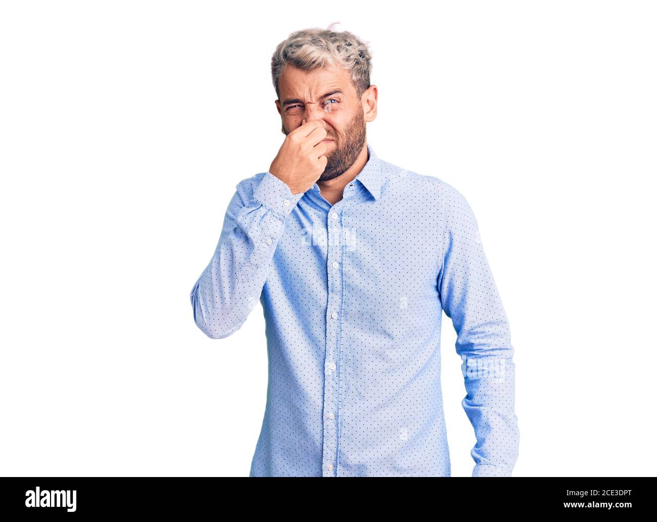 Young handsome blond man wearing elegant shirt smelling something ...