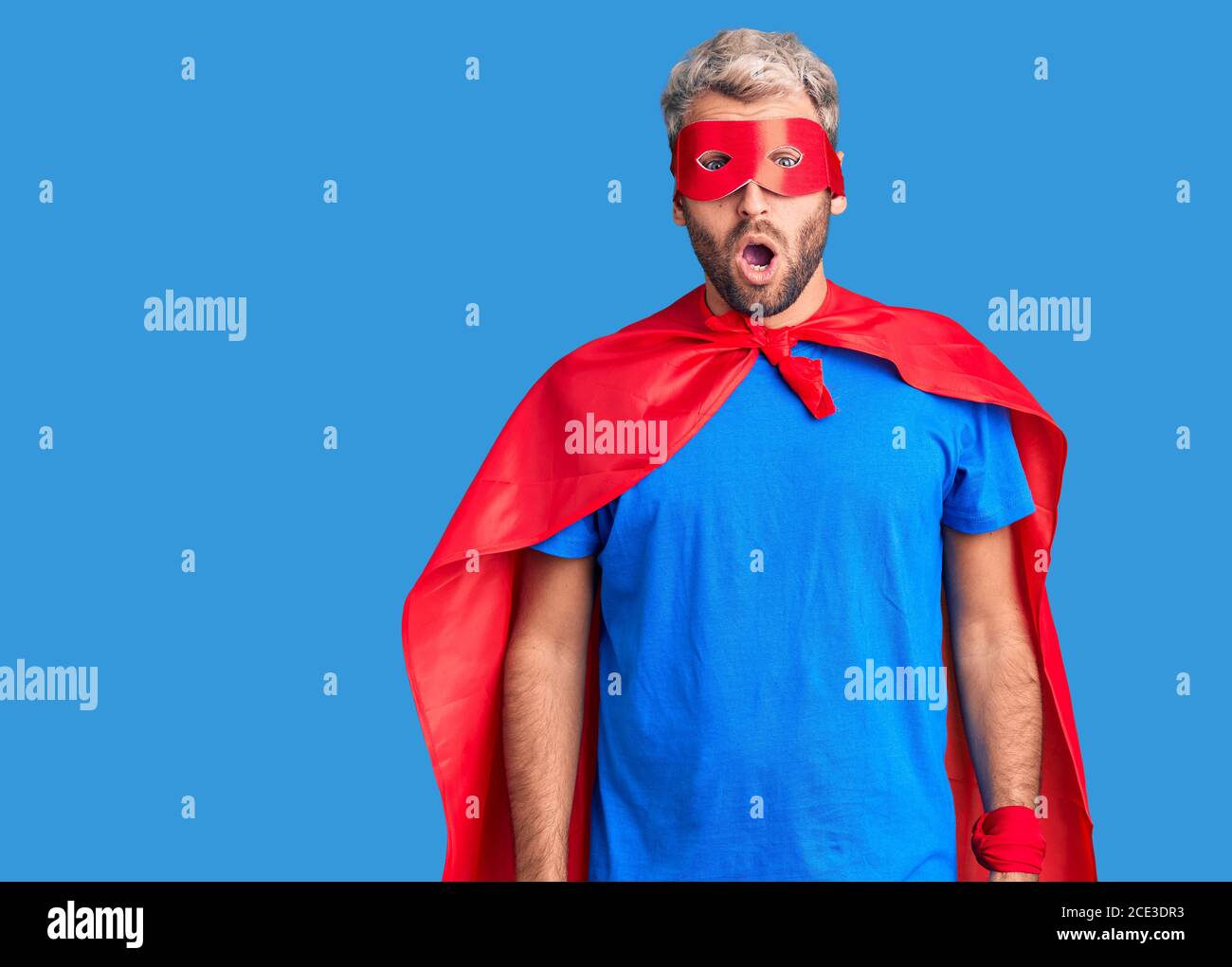 Young blond man wearing super hero custome afraid and shocked with ...