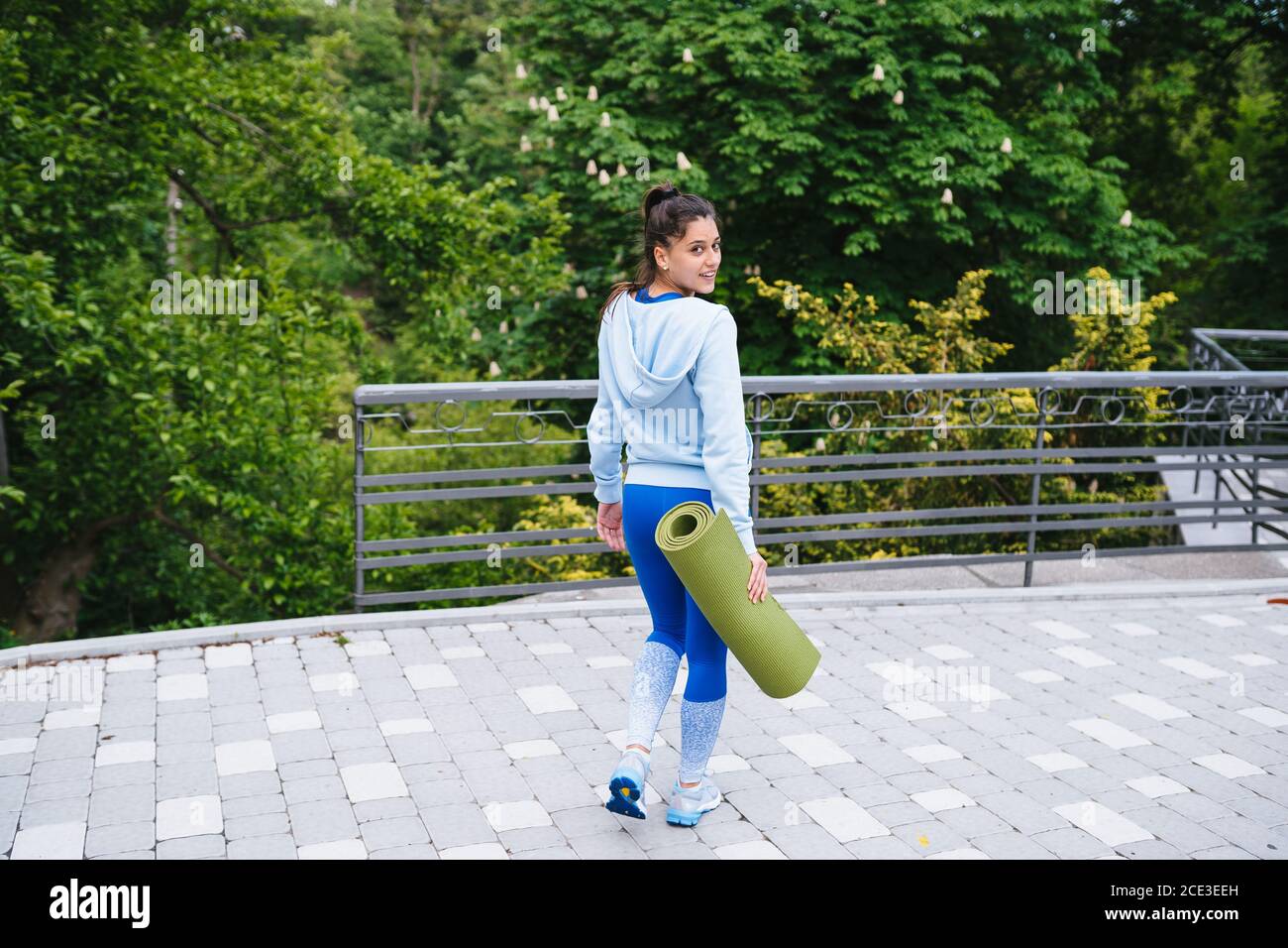 Young woman walking in urban park holding fitness rug Stock Photo - Alamy