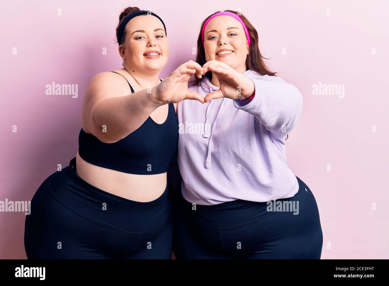 Young plus size twins wearing sportswear smiling in love doing heart ...