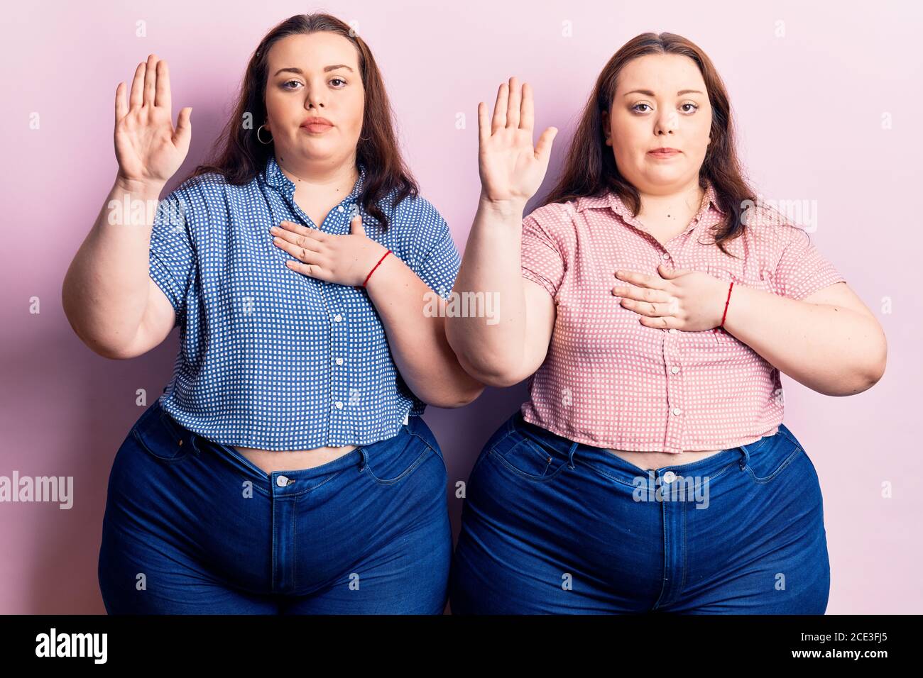 Young plus size twins wearing casual clothes swearing with hand on ...