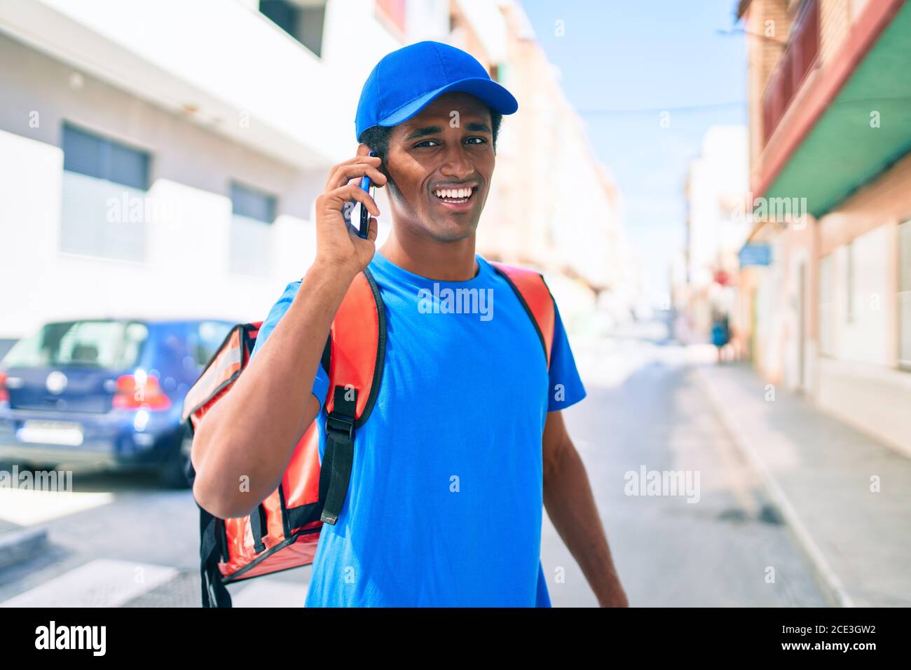 African delivery man wearing courier uniform outdoors speaking on the ...