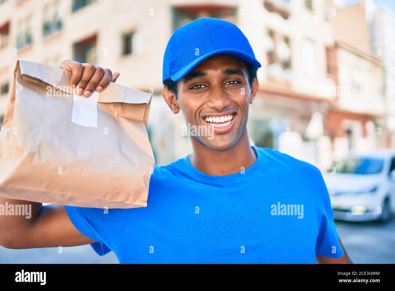 African delivery man wearing courier uniform outdoors holding take away ...