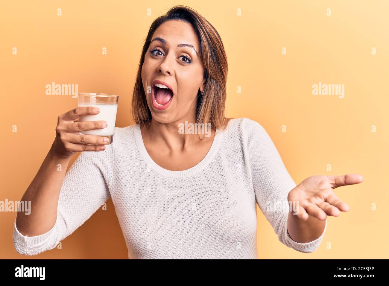 Young beautiful woman holding glass of milk celebrating achievement ...