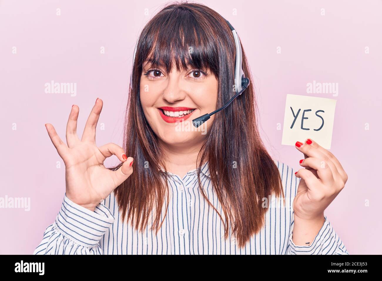 Young plus size woman wearing call center agent headset holding yes ...
