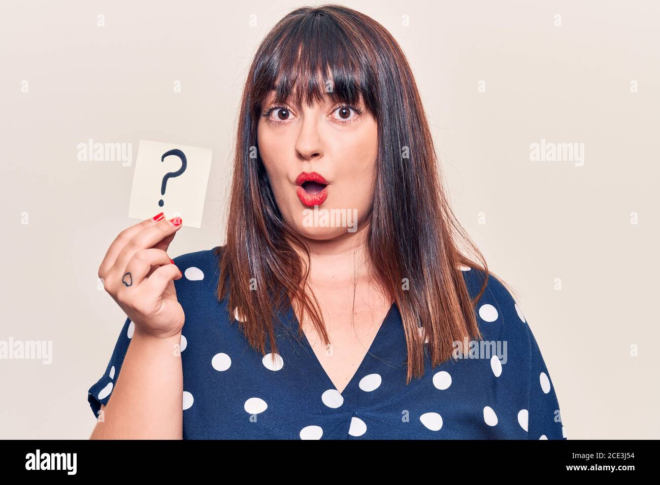 Young plus size woman holding question mark scared and amazed with open ...