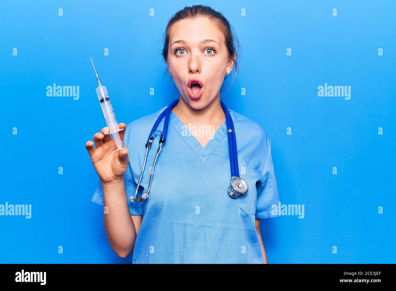 Young blonde woman wearing doctor uniform holding syringe scared and ...