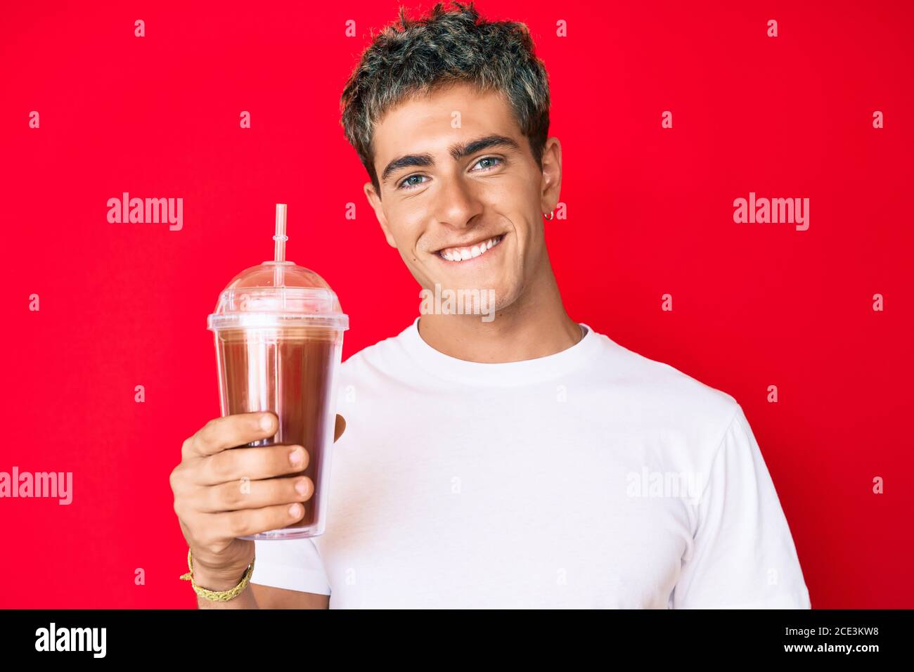 Young handsome man holding glass of smoothie looking positive and happy ...