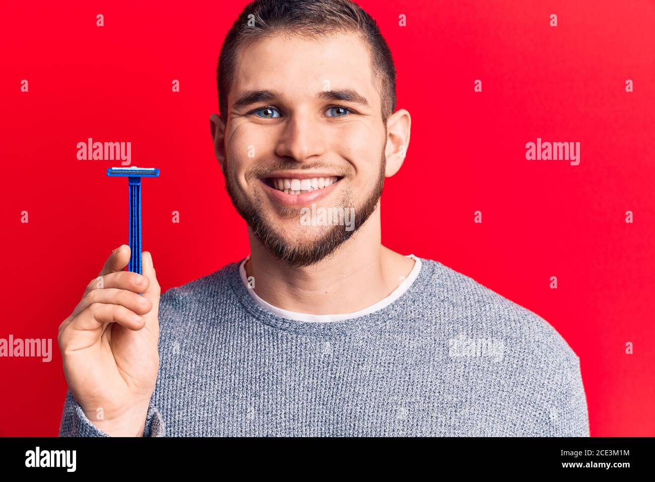 Young handsome man holding shave razor looking positive and happy ...