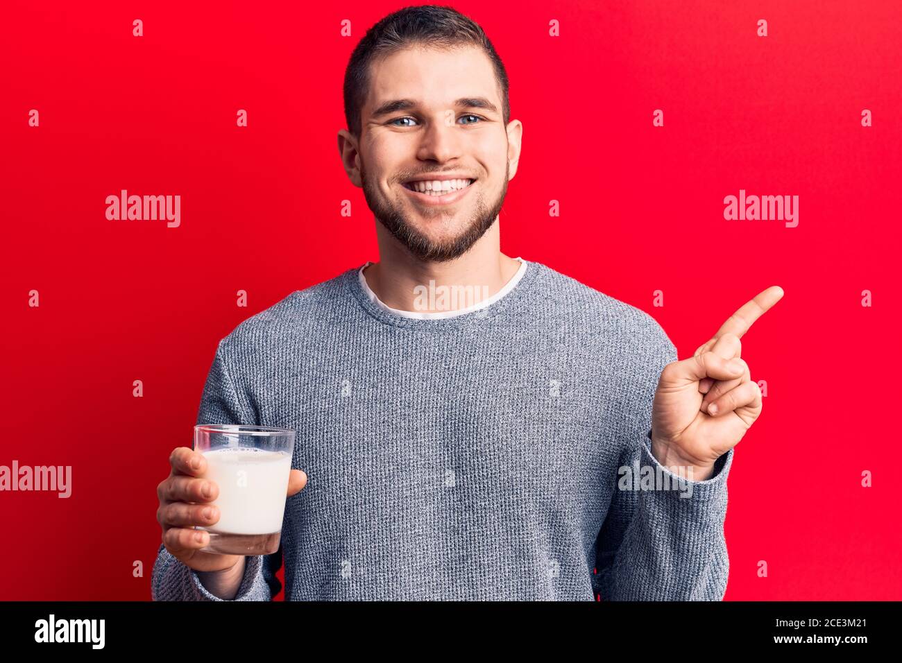 Young handsome man drinking glass of milk smiling happy pointing with ...