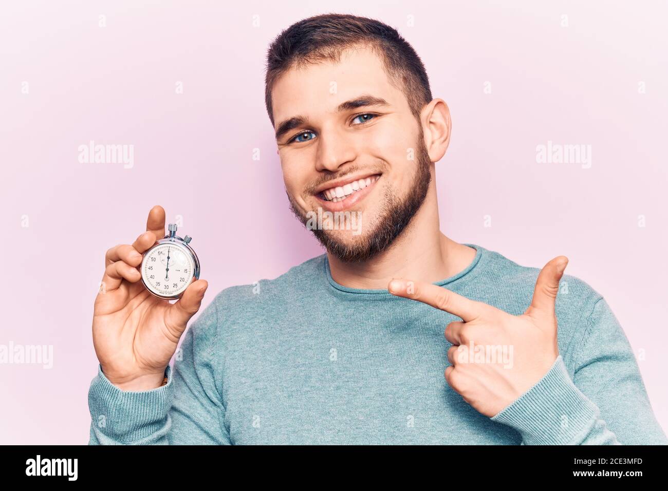 Young handsome man holding stopwatch smiling happy pointing with hand ...