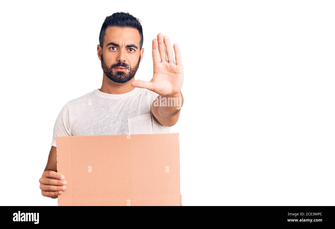 Young hispanic man holding banner cardboard with open hand doing stop ...
