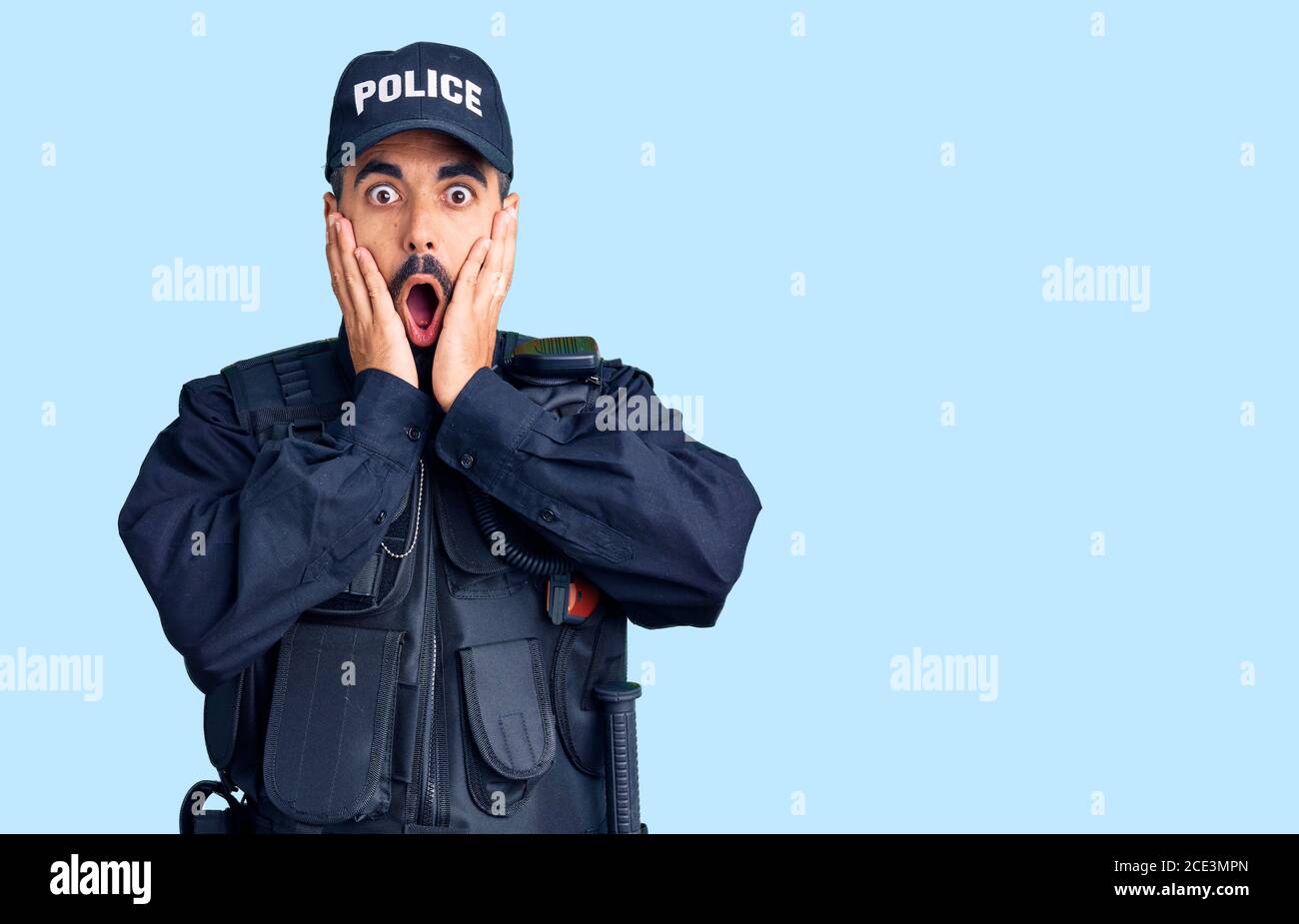 Young hispanic man wearing police uniform afraid and shocked, surprise ...