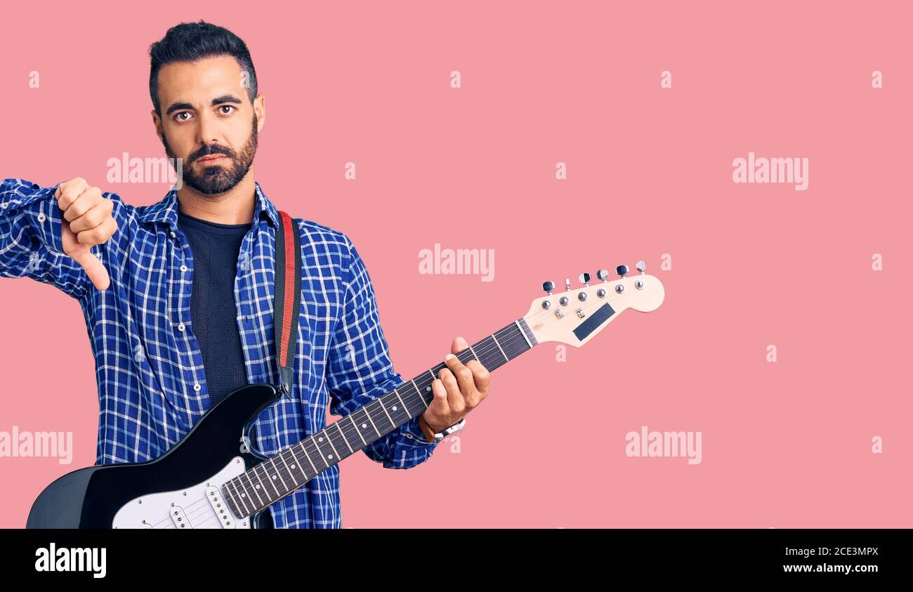 Young hispanic man playing electric guitar with angry face, negative ...