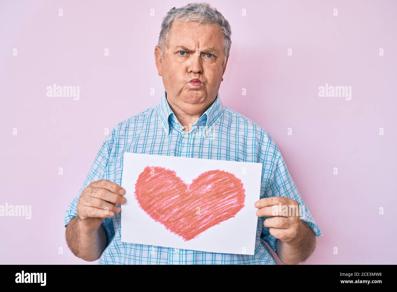 Senior grey-haired man holding heart draw puffing cheeks with funny ...