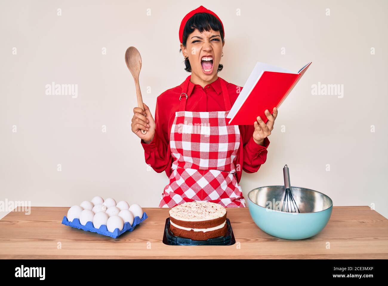 Beautiful brunettte woman cooking cake reading recipes book angry and ...