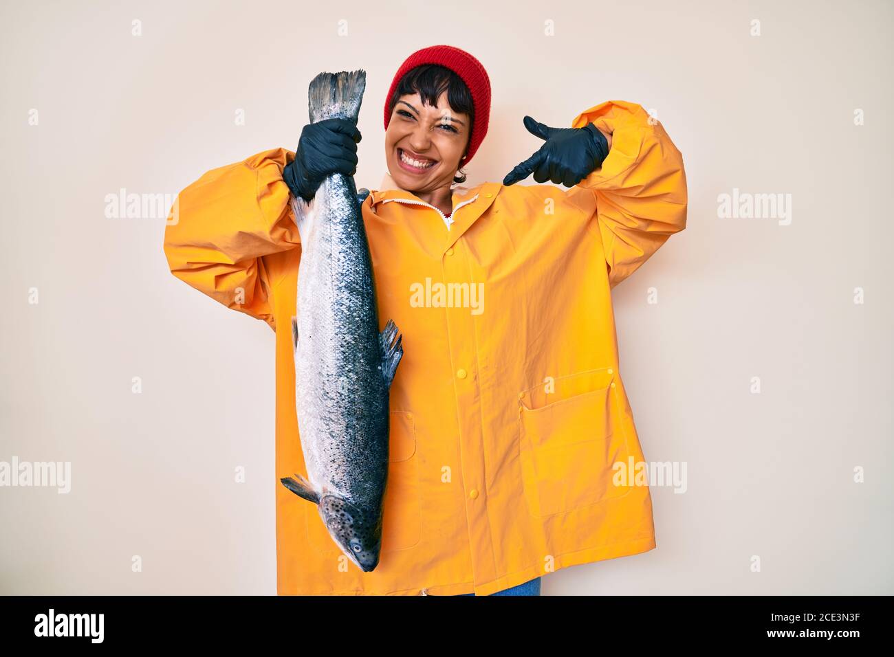 Beautiful brunettte fisher woman wearing raincoat holding fresh salmon ...
