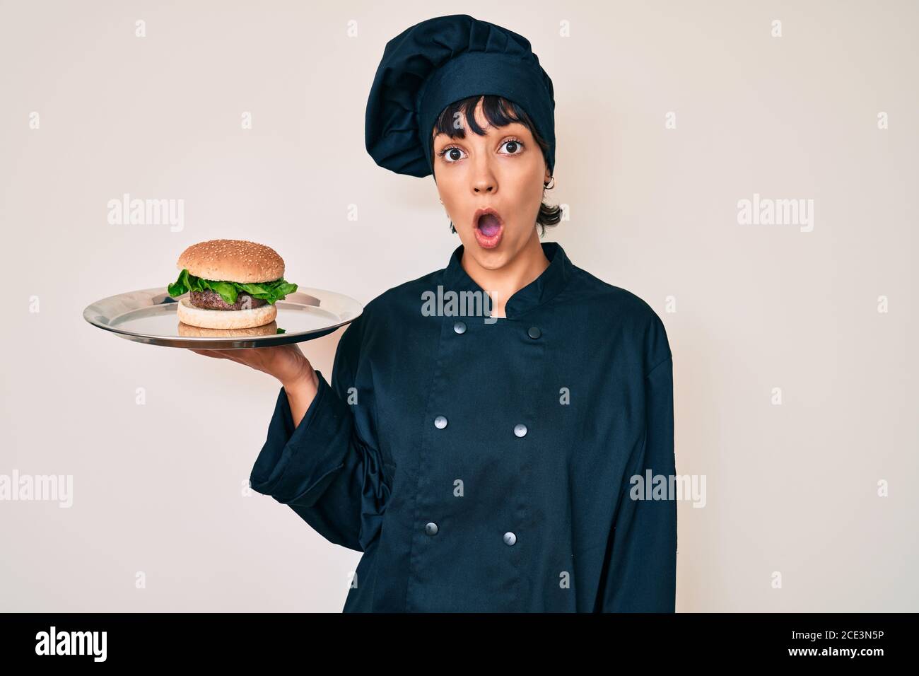 Beautiful brunettte woman chef holding burguer scared and amazed with ...