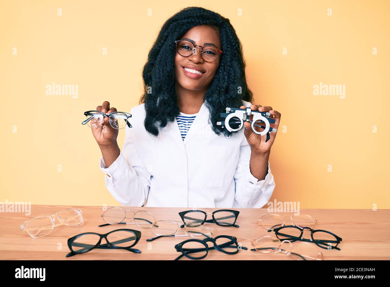 Young african american woman wearing optician uniform holding glasses ...