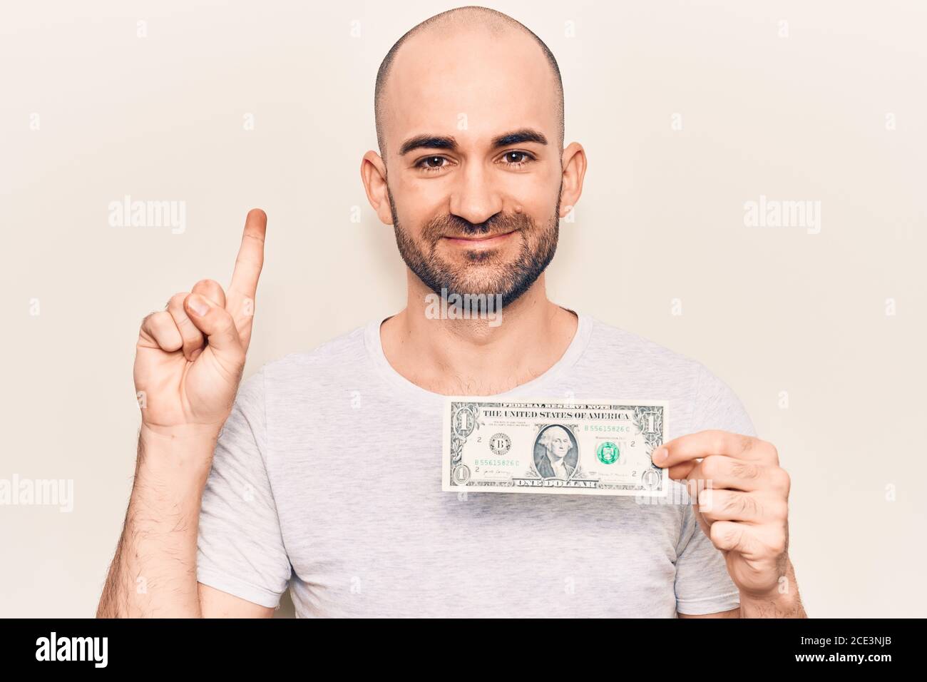 Young handsome bald man holding one dollar banknote smiling with an ...