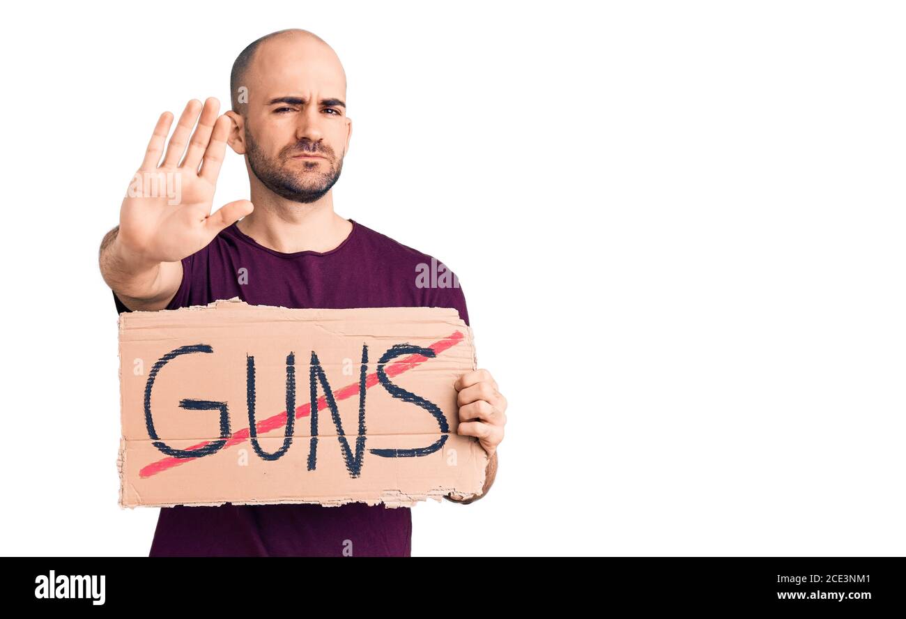 Young handsome man holding prohibited guns banner with open hand doing ...