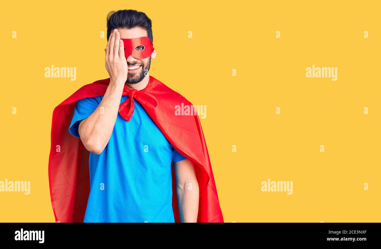 Young handsome man with beard wearing super hero costume covering one ...