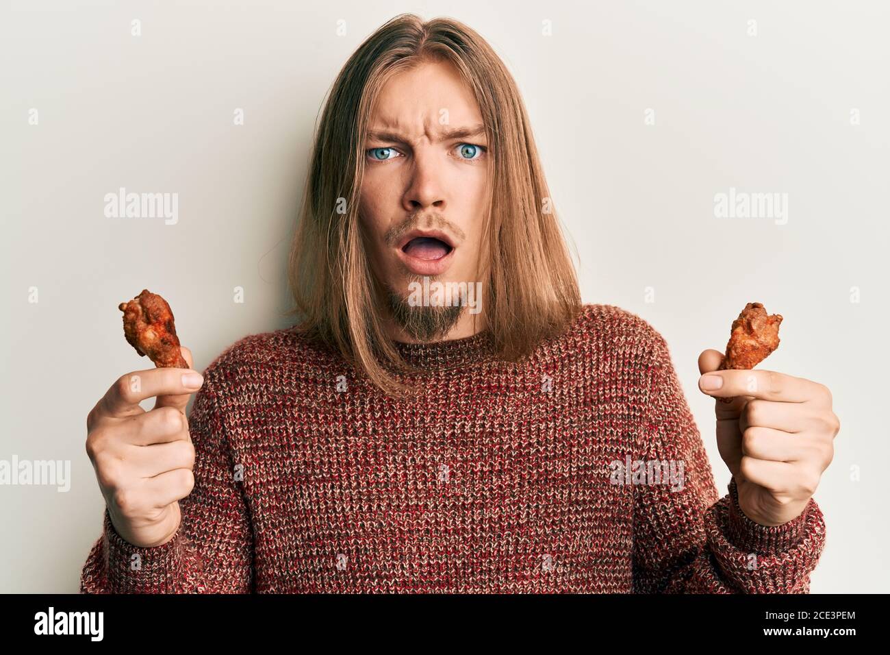 Handsome caucasian man with long hair eating chicken wings in shock ...