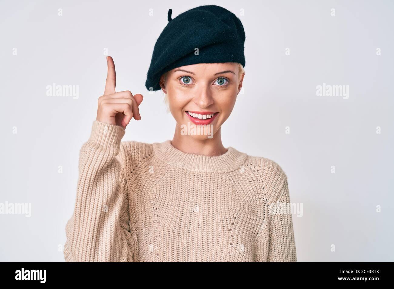 Young blonde woman wearing french look with beret pointing finger up ...