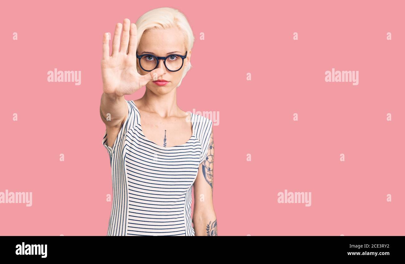 Young blonde woman with tattoo wearing casual clothes and glasses doing ...