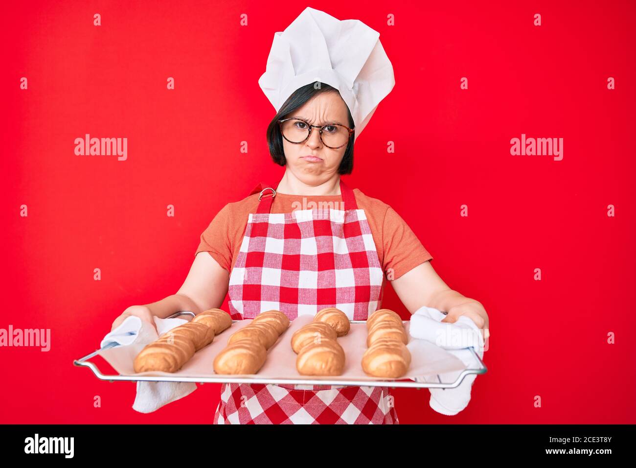 Brunette woman with down syndrome wearing baker uniform holding ...