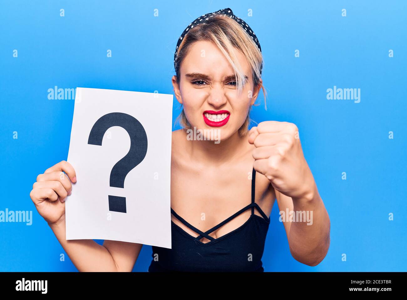 Young beautiful blonde woman holding question mark annoyed and ...