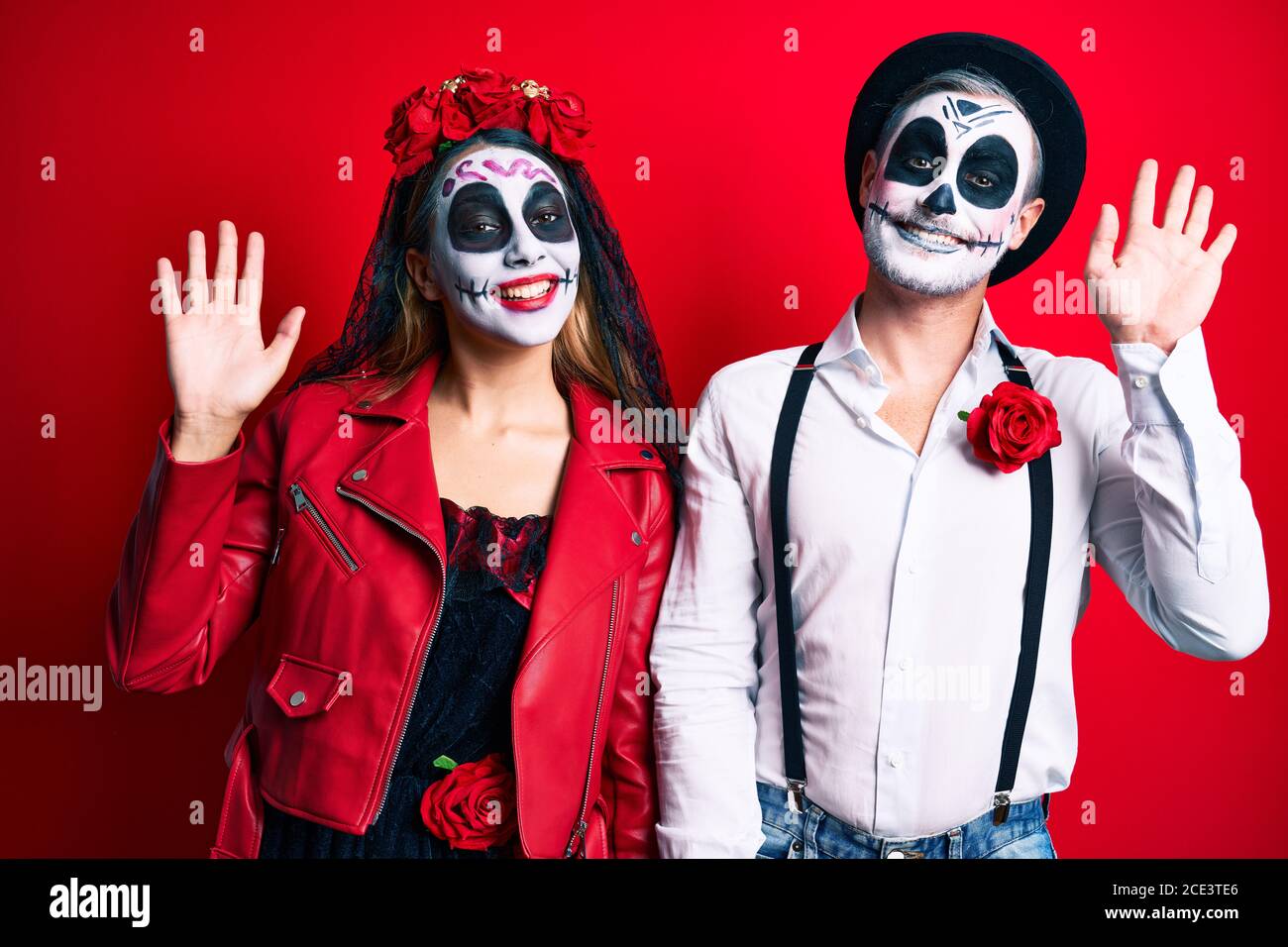 Couple wearing day of the dead costume over red waiving saying hello ...