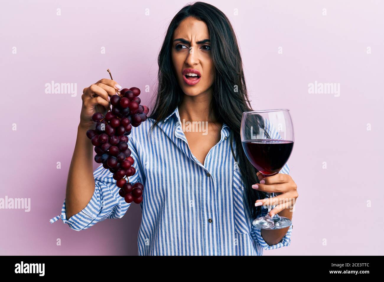 Beautiful hispanic woman holding branch of fresh grapes and red wine ...