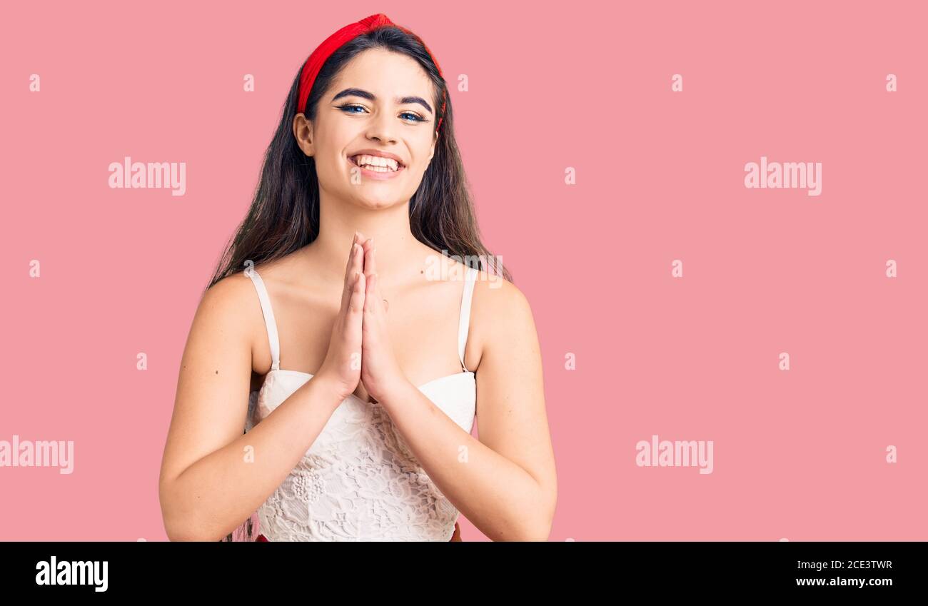 Brunette teenager girl wearing elegant look praying with hands together ...