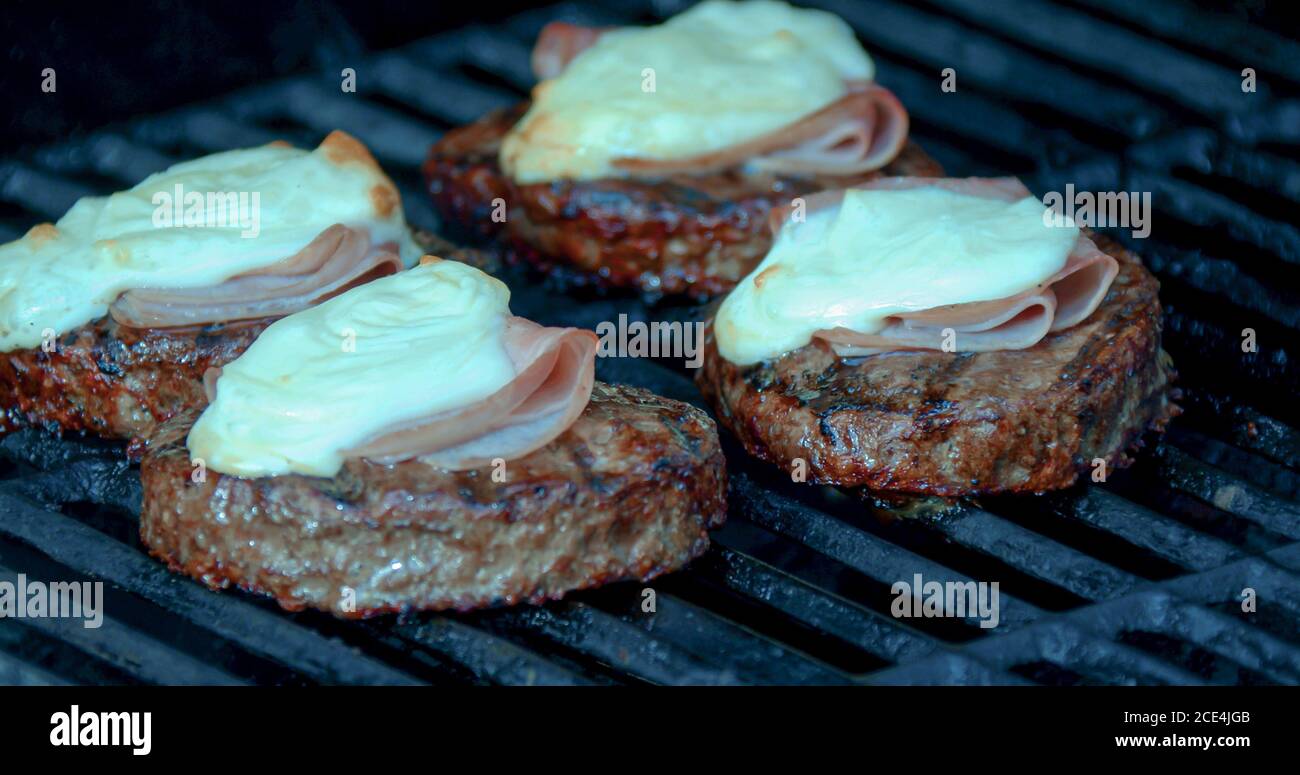 Cooking a burger patty with melted cheese and ham on a grill Stock ...