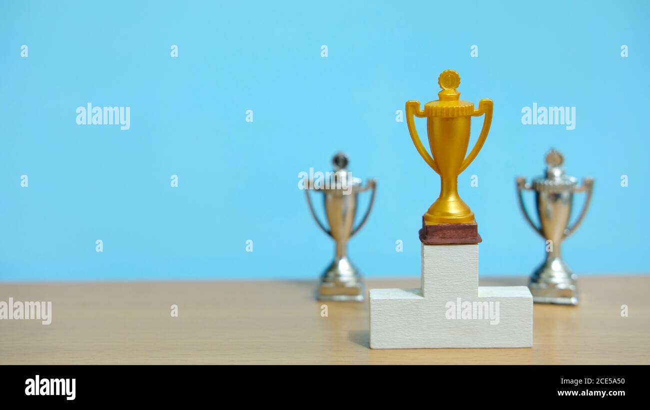 Golden trophy standing on white podium with two silver trophy at back ...