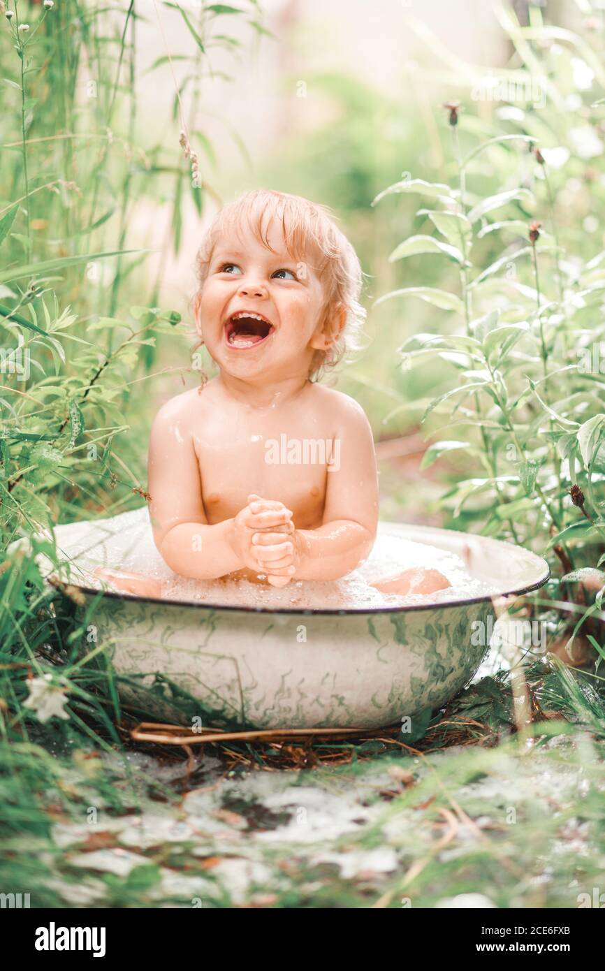 Cute funny little boy bathing in galvanized tub outdoor in green garden ...