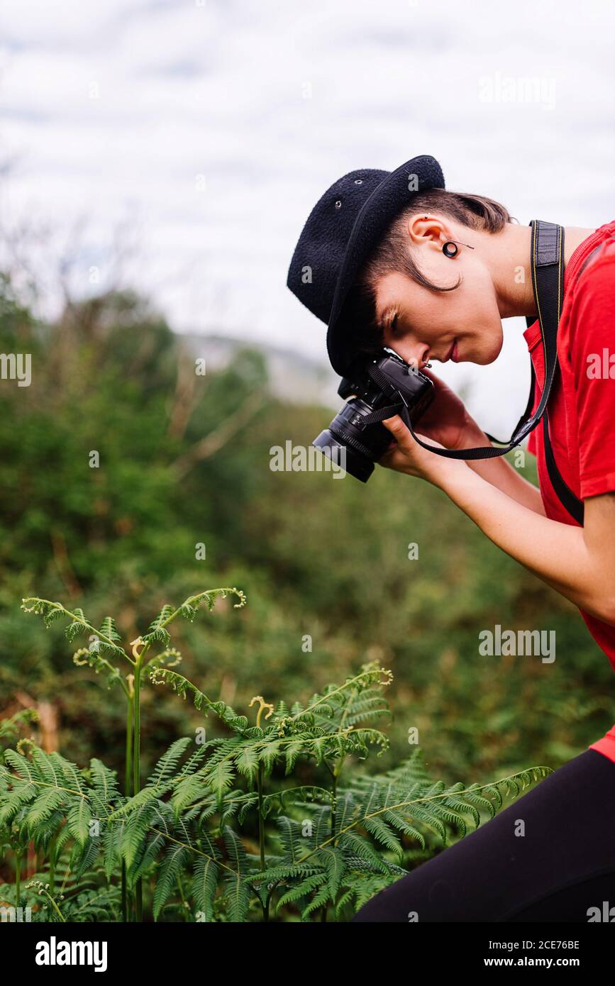 Side view of talented female photographer in trendy outfit taking photo ...
