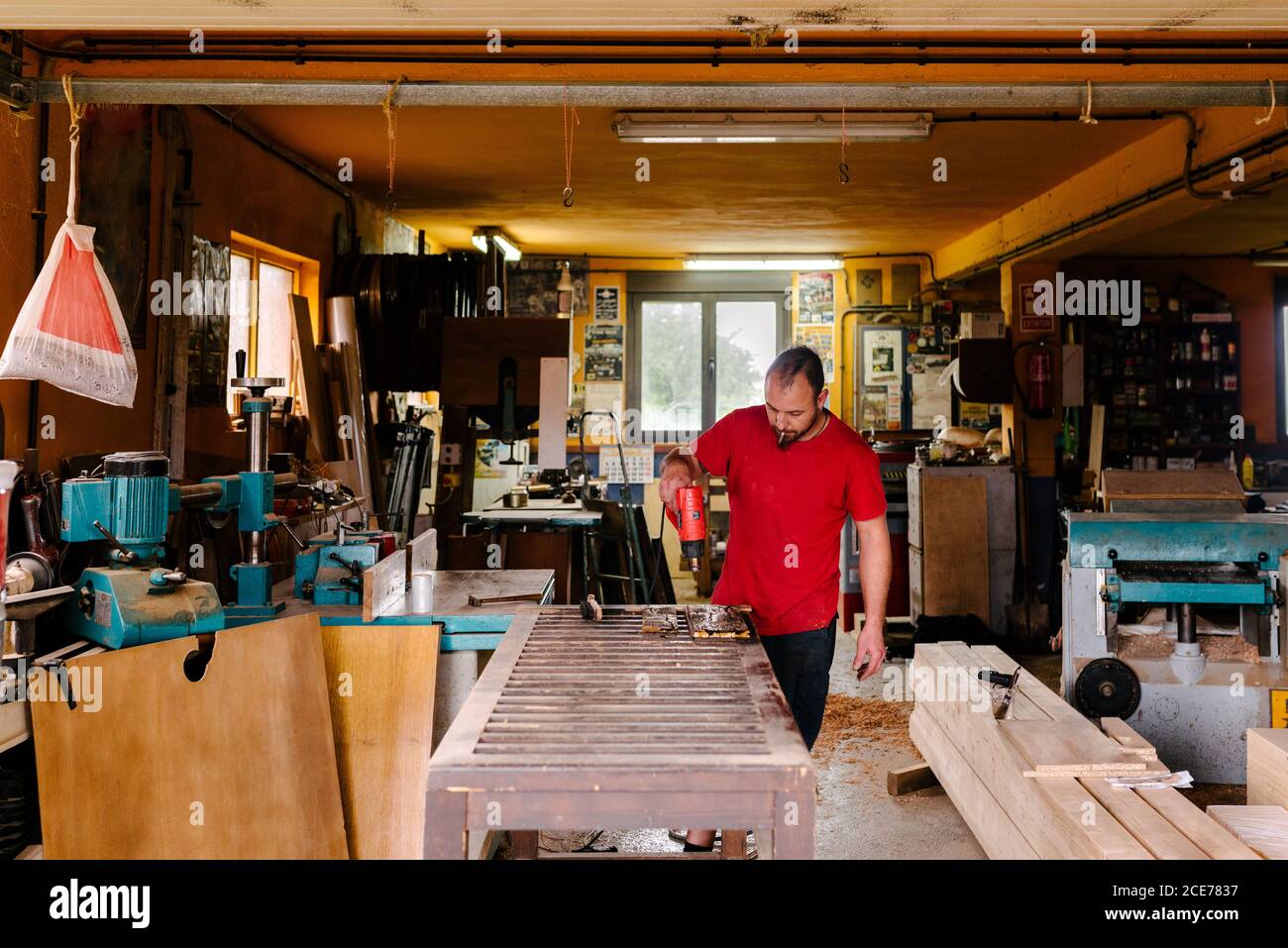 Serious male woodworker standing in shabby workshop and drying timber ...