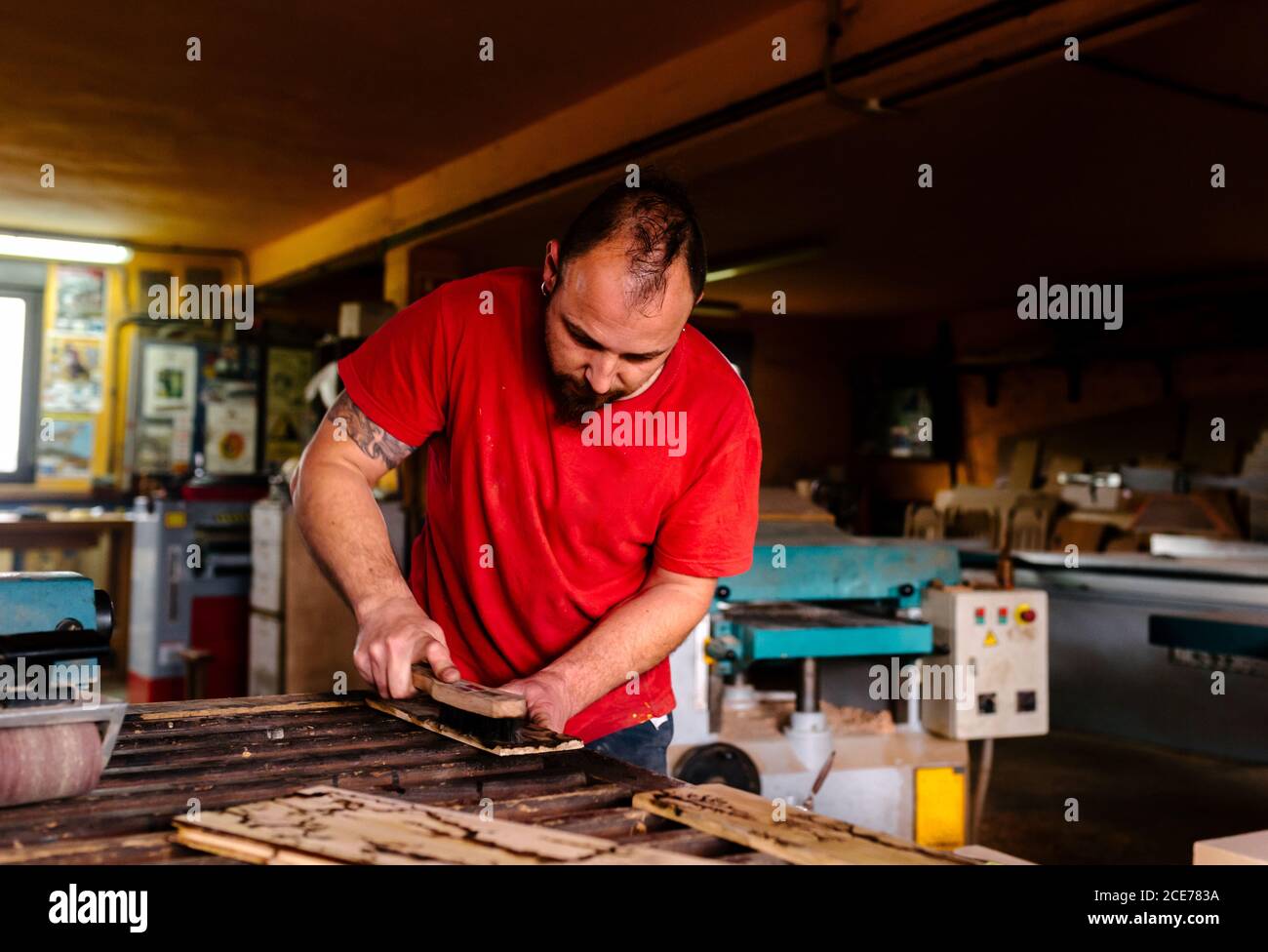 Busy male woodworker standing at workbench and polishing timber plank ...