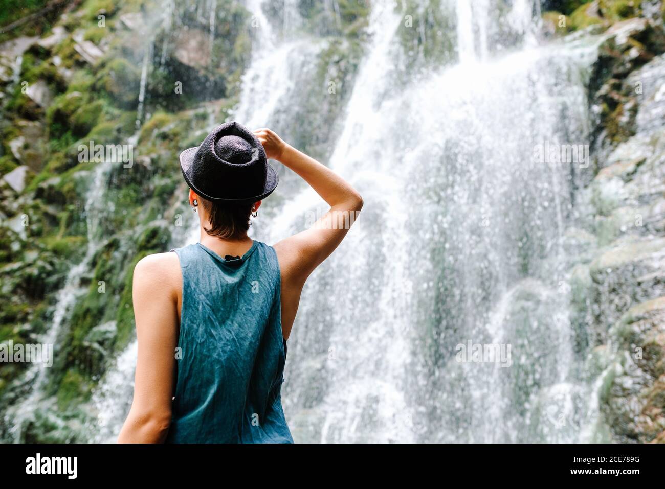 Low angle back view of androgynous female tourist standing on rock and ...