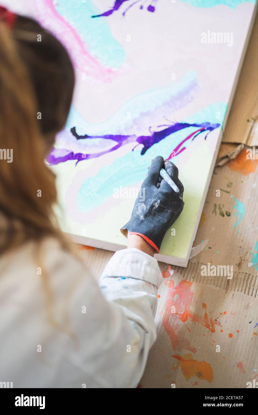 Crop anonymous female illustrator in dirty robe and gloves sitting on ...