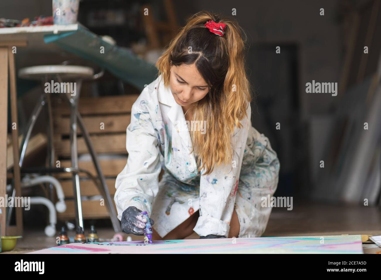 Cheerful barefoot female artist in dirty robe and gloves lying on ...