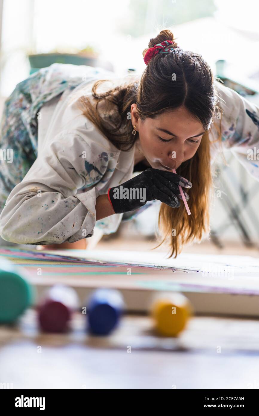 From above of female painter in dirty robe and gloves blowing through ...