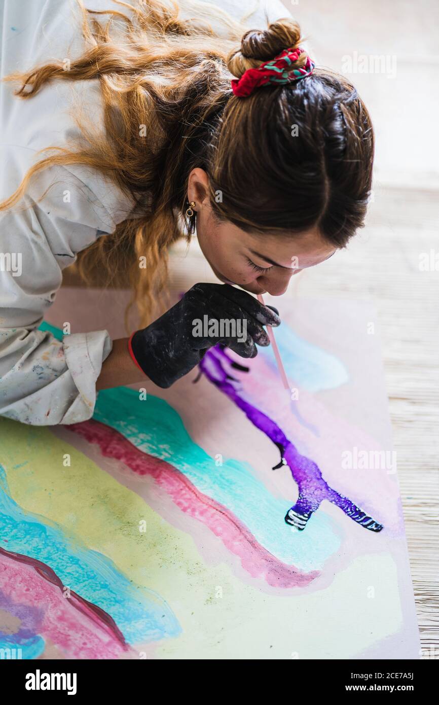 From above of female painter in dirty robe and gloves blowing through ...