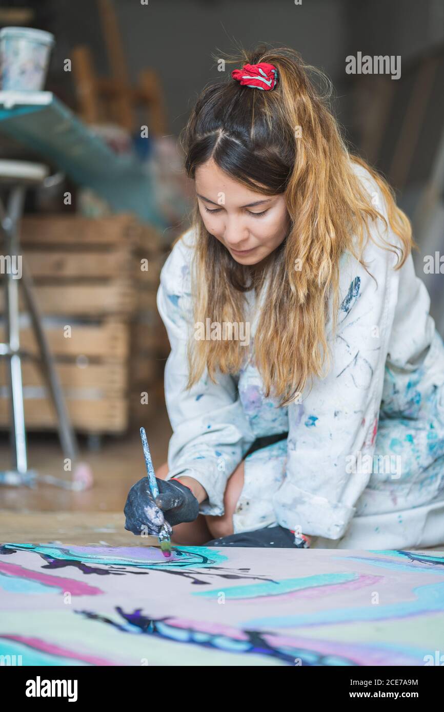 Cheerful barefoot female artist in dirty robe and gloves lying on ...