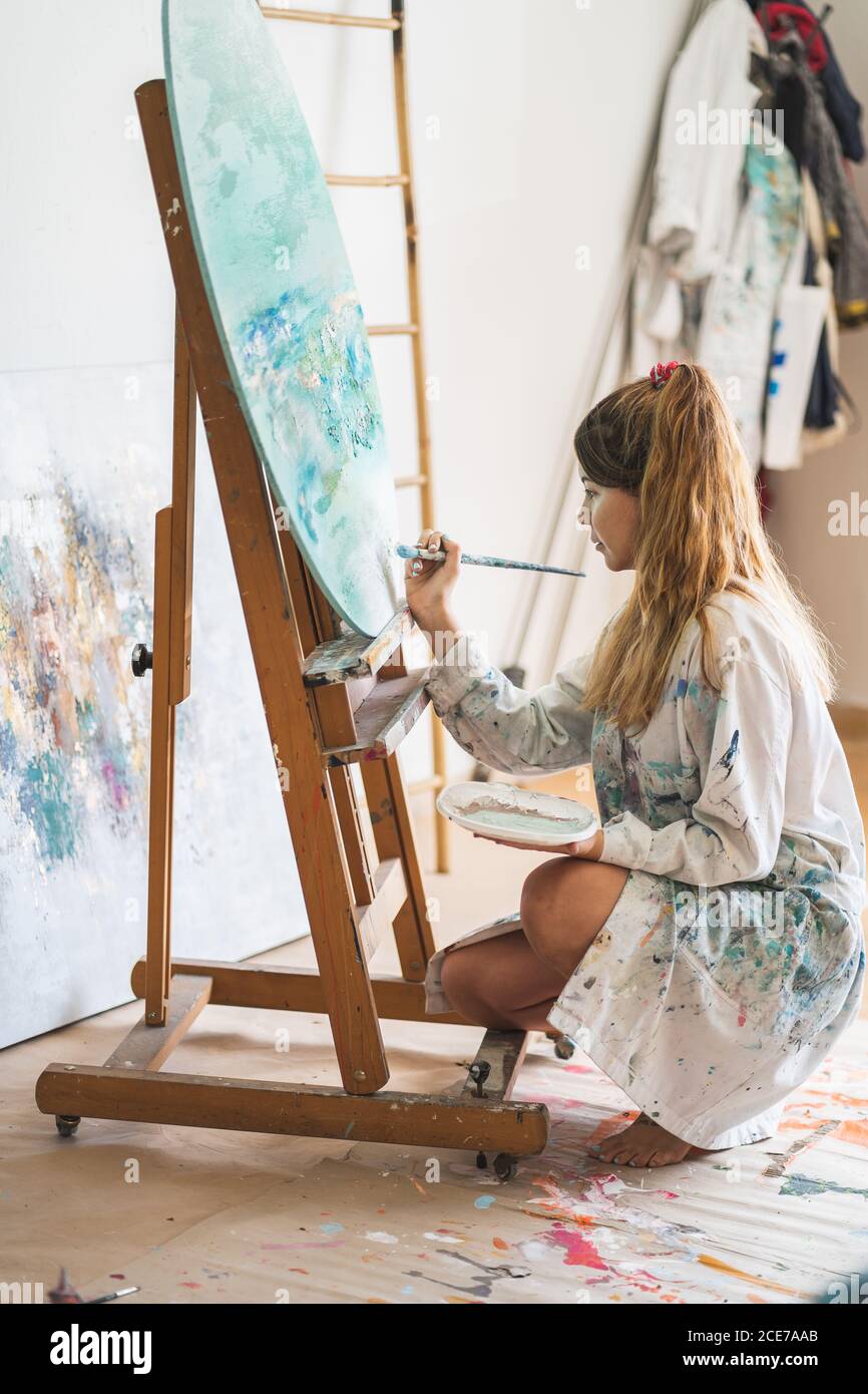 Side view female master in dress smeared with paint painting seascape ...
